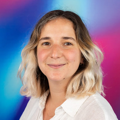 Person with long dark hair wearing lavender cardigan smiling at camera